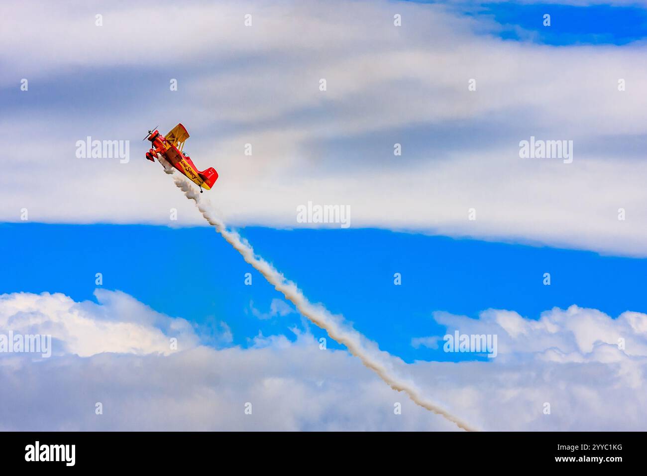 A red and yellow plane is flying through the sky with smoke trailing ...