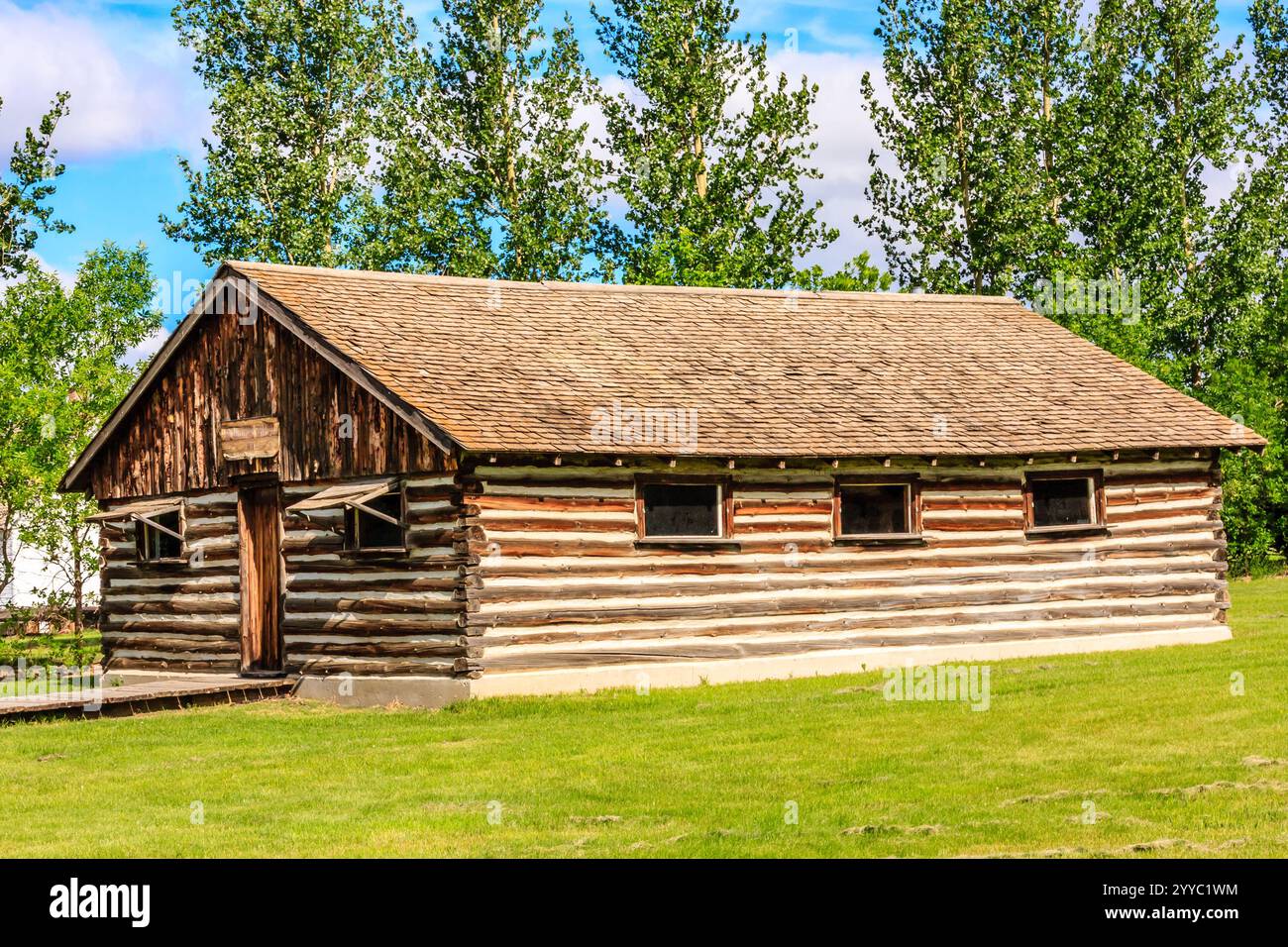A log cabin with a slanted roof sits on a grassy field. The cabin is ...