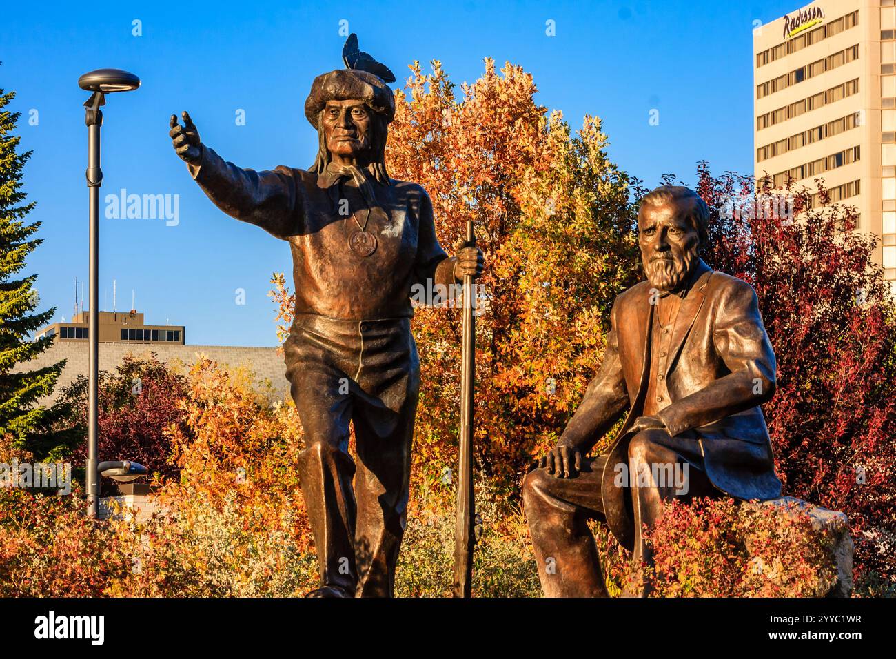 Two statues of men sitting on a bench in a park. One of the statues is ...