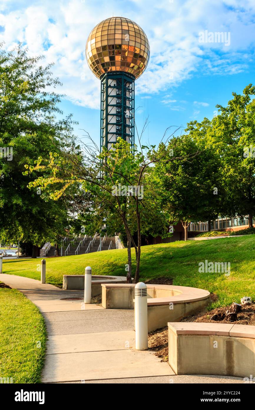 A large, gold-colored ball sits atop a tall tower in a park. The park ...