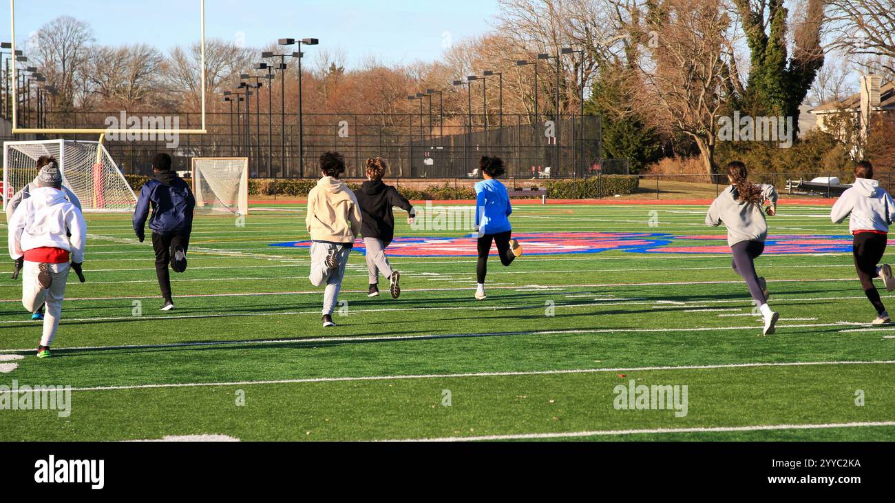 A group of young athletes run swiftly on a turf field during afternoon ...