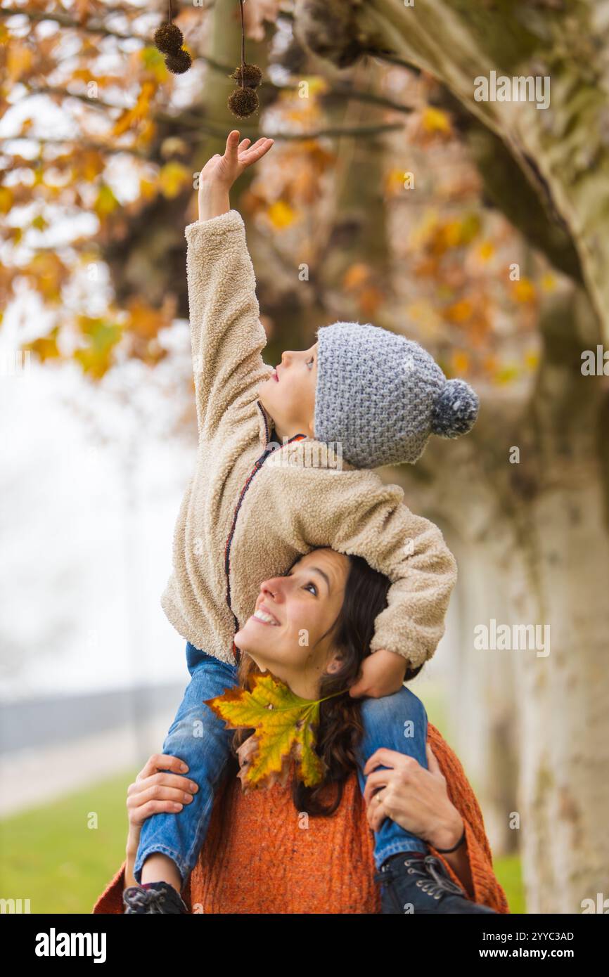 Child reaching for autumn tree branches while sitting on mother s ...