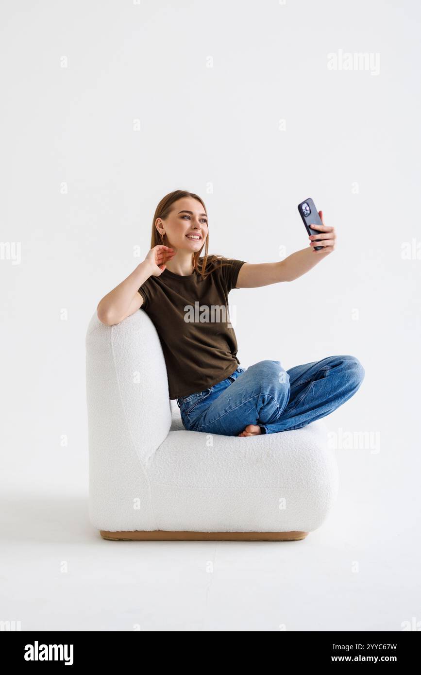 Pretty young woman with smartphone and coffee taking selfie while ...