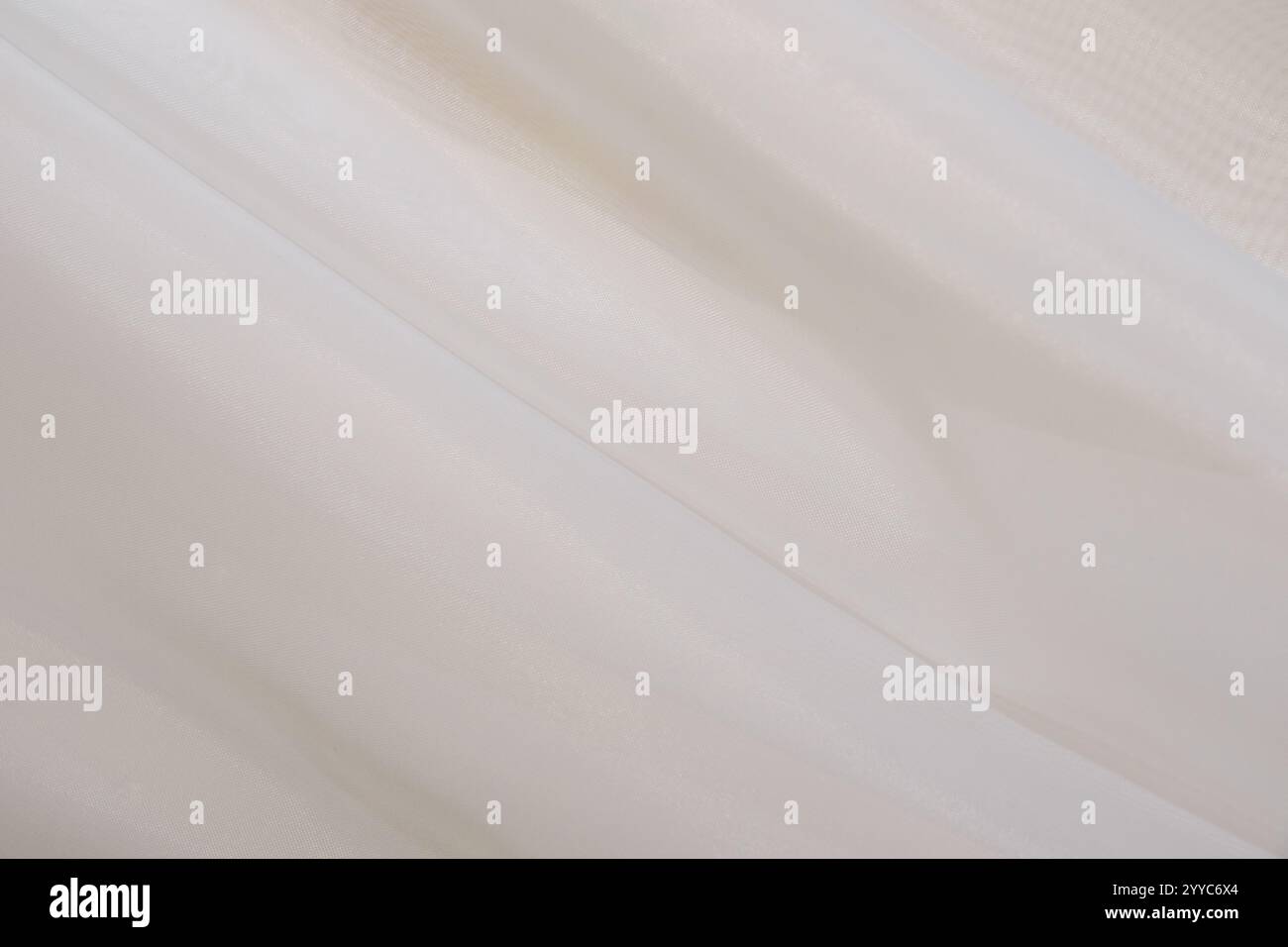 A soft beige fabric is gently draped across a smooth surface, illuminated by natural light. The ...