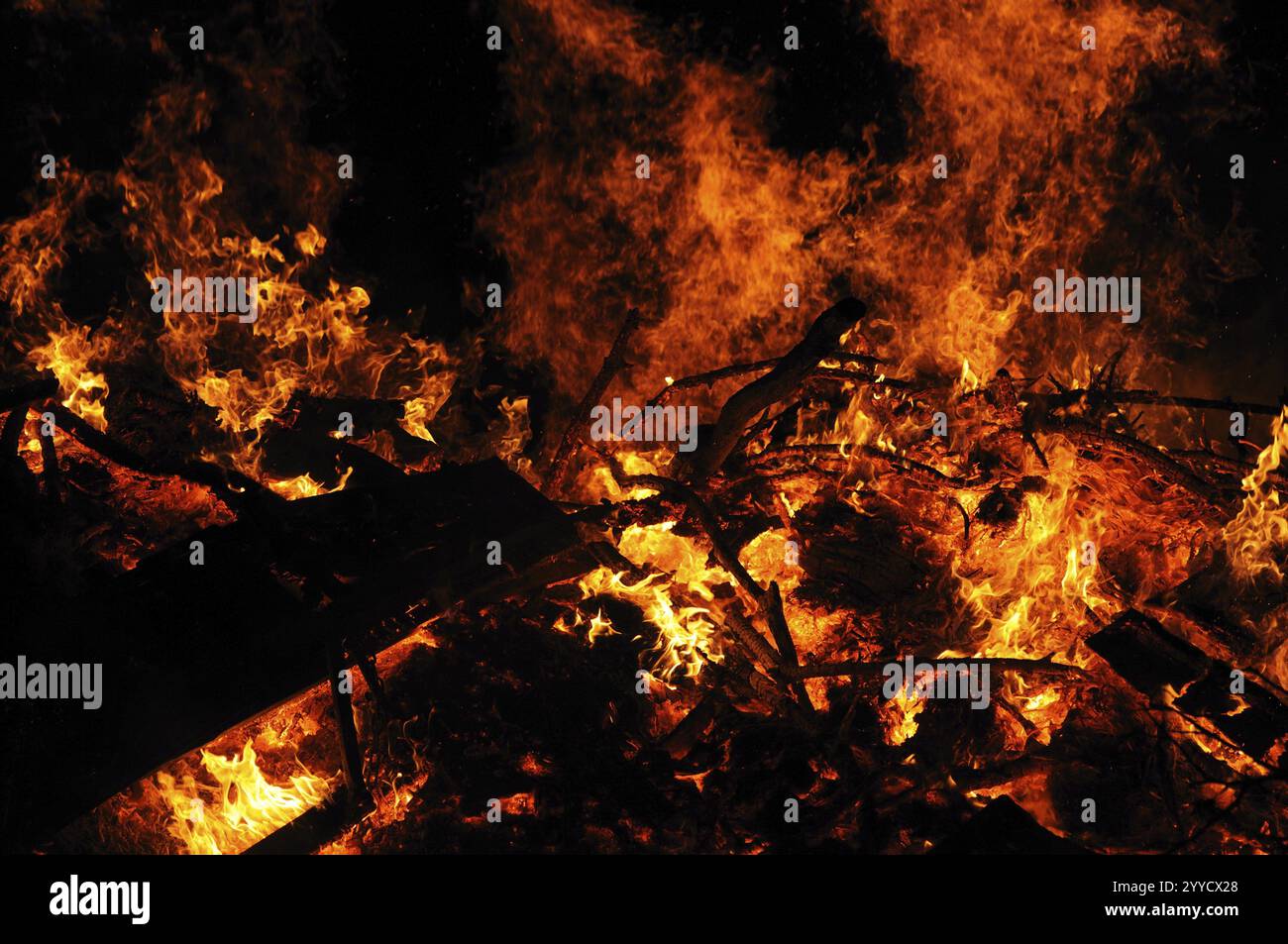 Intense flames and embers surround burning wood in the dark, campfire ...