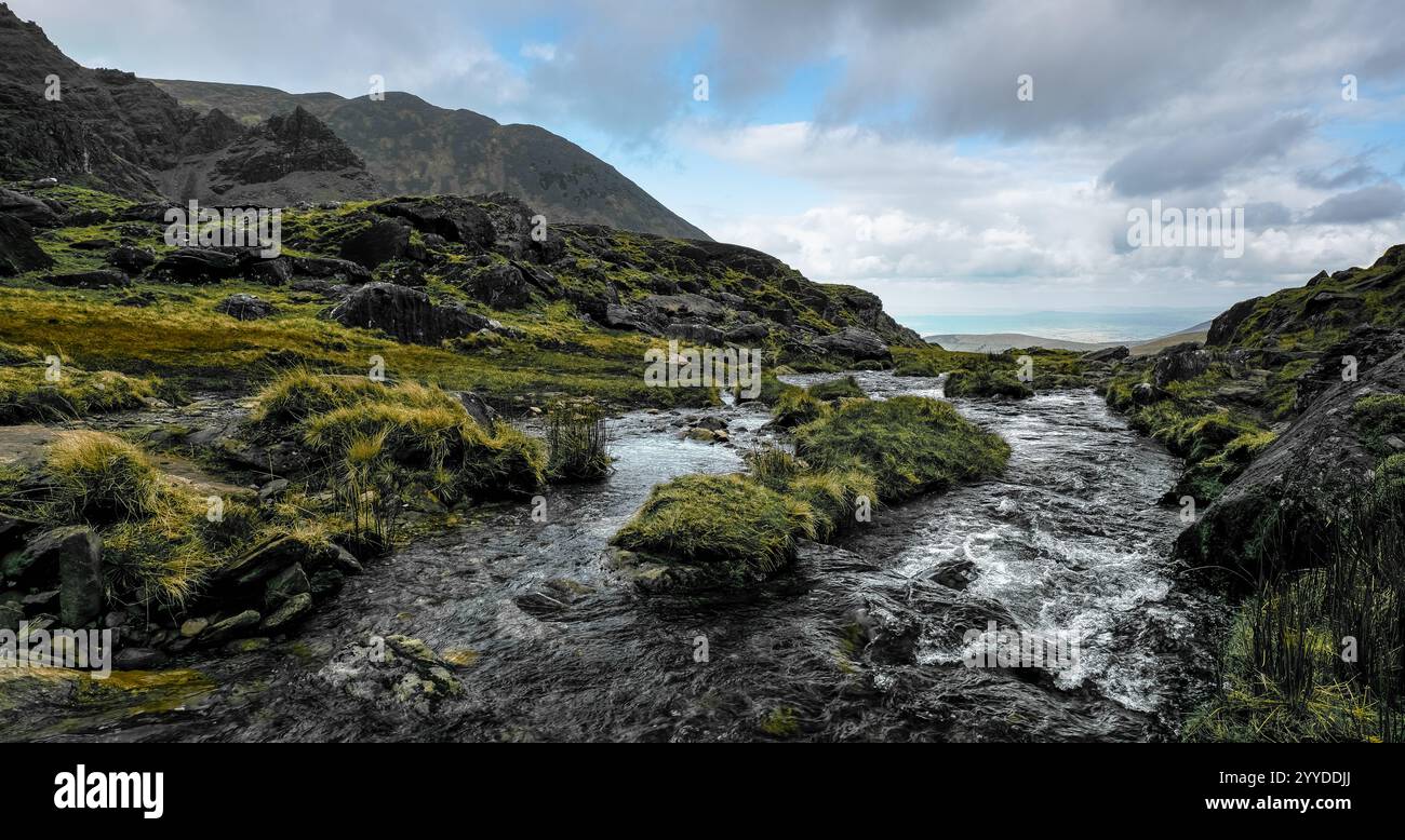 A small river cuts through a mountainous landscape. The water is ...