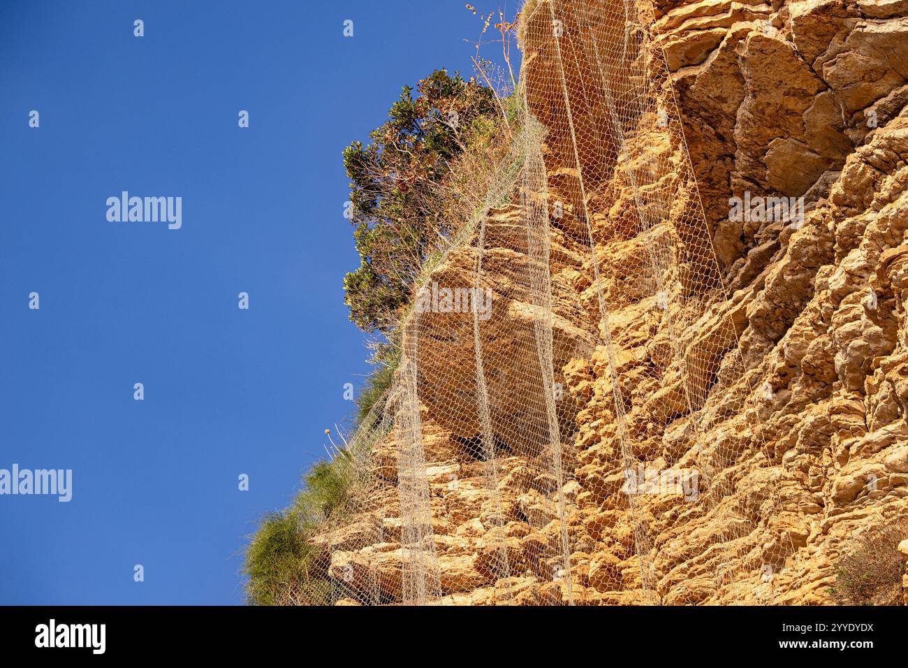 Metal mesh netting draped over a steep, rocky cliff face, preventing ...