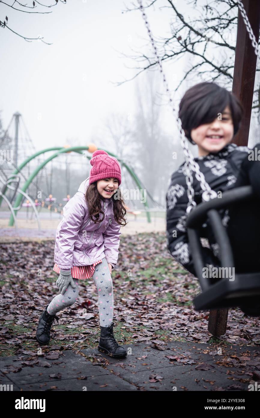 one smiling girl pushing the one one on the swing at children ...