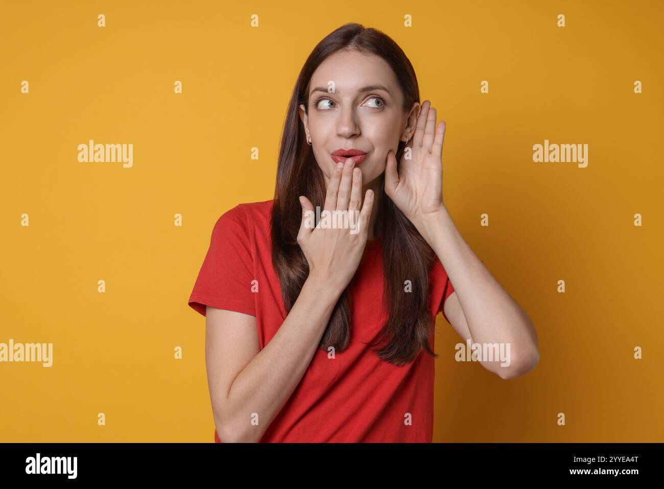 Woman showing hand to ear gesture on orange background Stock Photo - Alamy