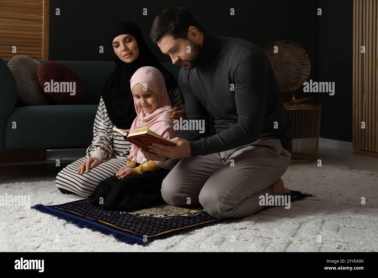 Muslim family with Quran praying on mat at home Stock Photo - Alamy