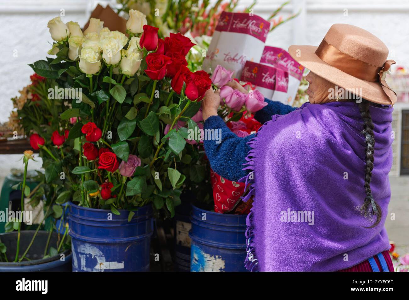 Woman in traditional attire arranging colorful roses in buckets at a ...