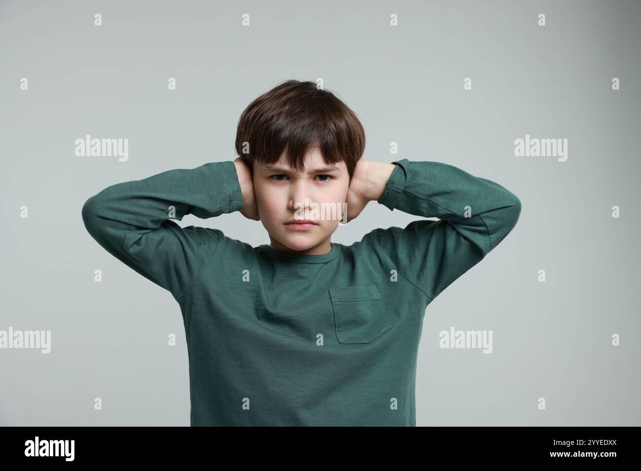 Annoyed boy covering his ears due to loud sound on grey background ...