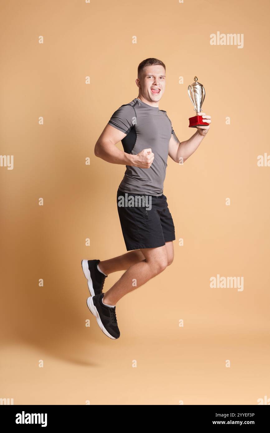 Happy winner with golden trophy cup jumping on beige background Stock ...