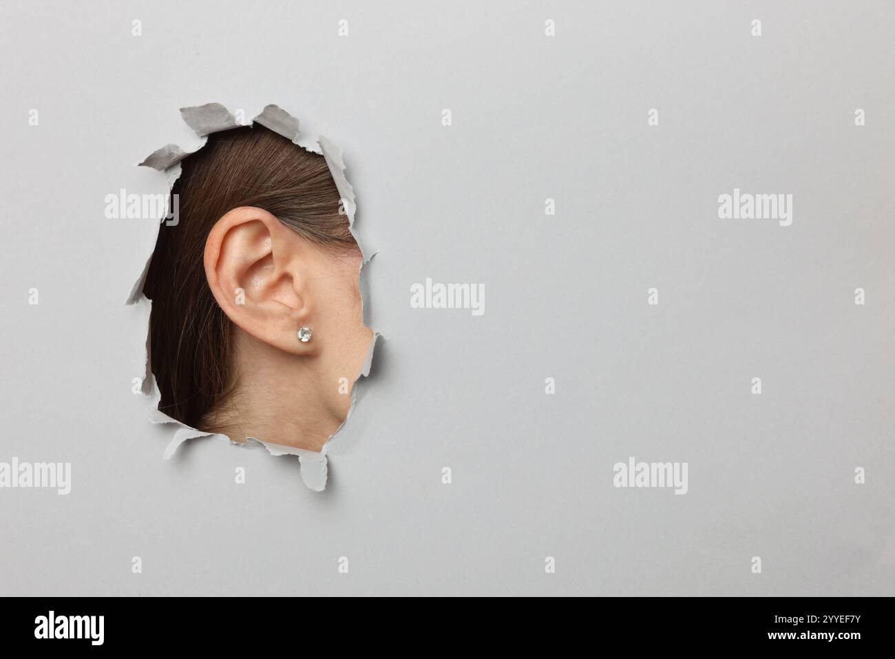 Woman showing her ear through hole in grey paper, closeup. Space for ...