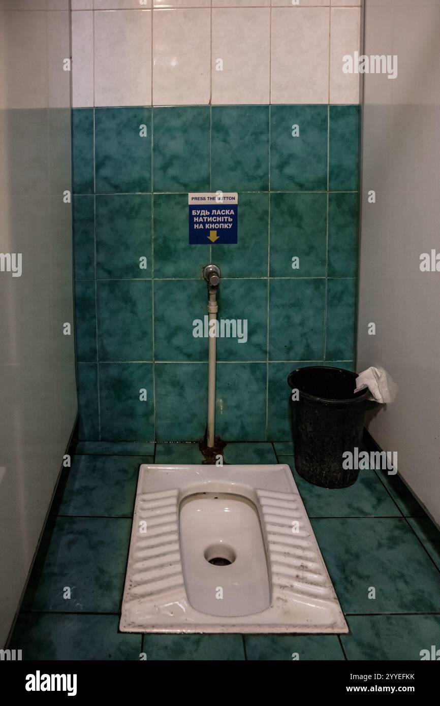A small bathroom with a squat toilet and a sign that says "No Standing ...