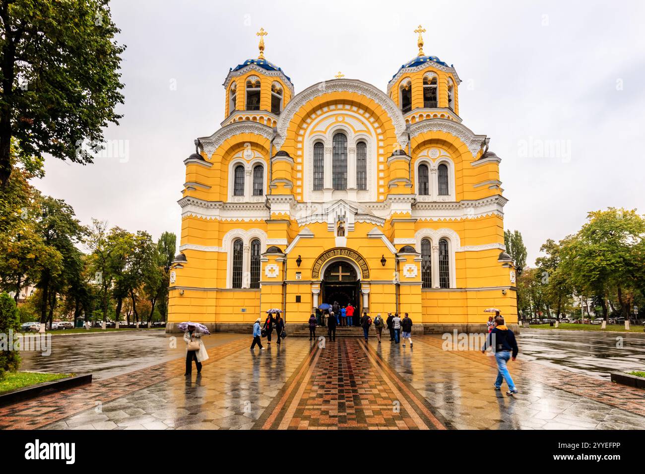 A large yellow church with a blue cross on top. People are walking in ...