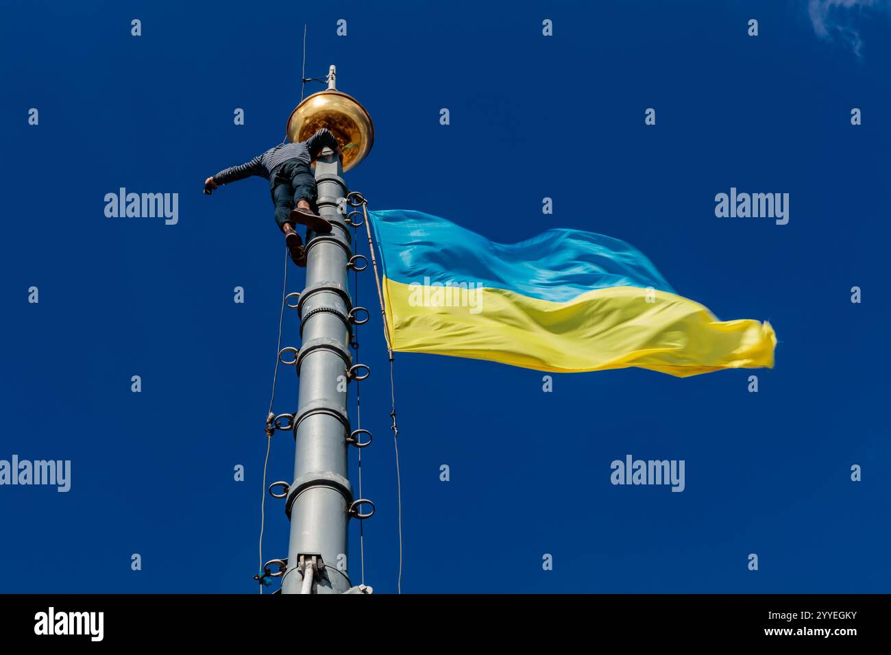 A man is climbing a pole to reach a flag. The flag is yellow and blue ...