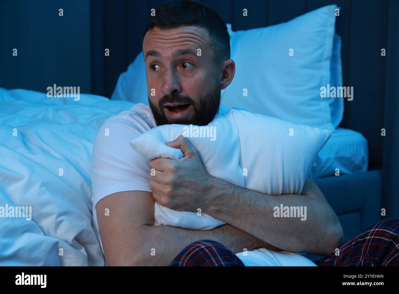 Fear of darkness. Scared man hugging pillow in bedroom at night Stock ...