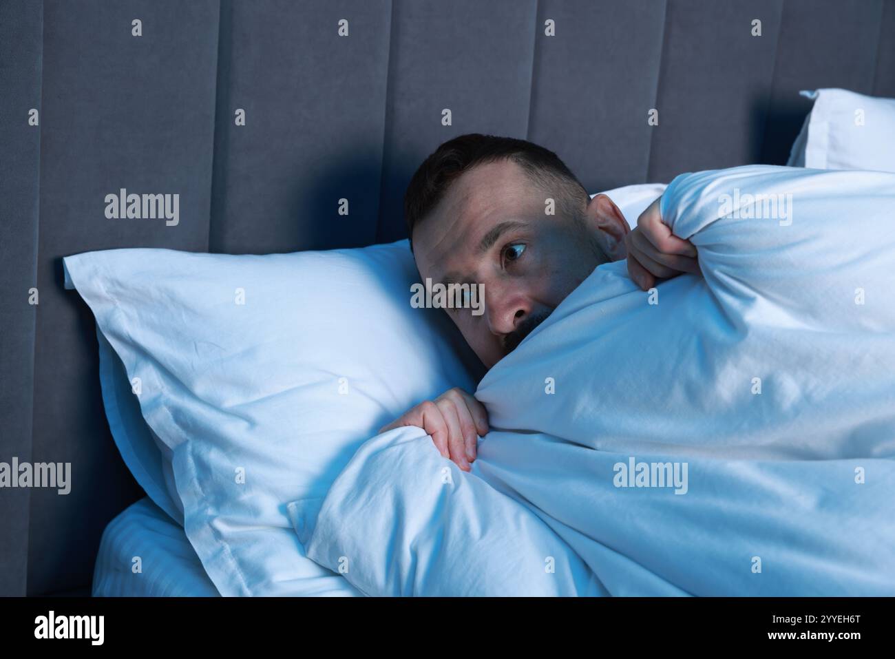 Fear of darkness. Scared man lying on bed in room at night Stock Photo ...