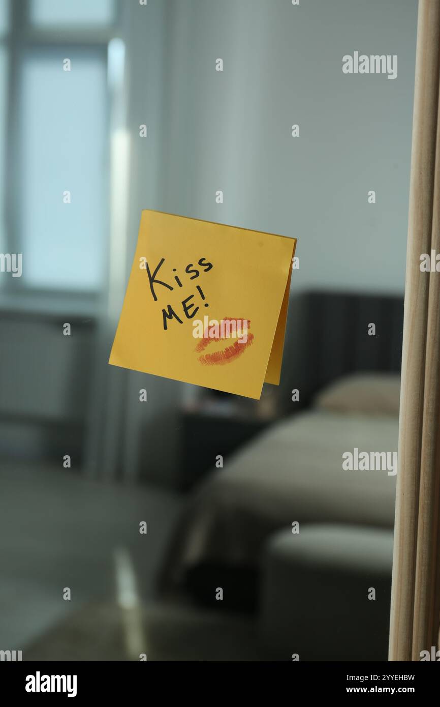 Sticky note with phrase Kiss Me and lipstick mark attached to mirror in ...
