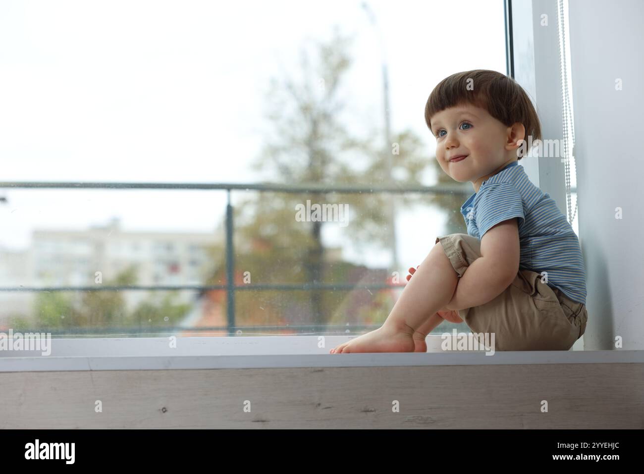 Little boy sitting on window sill, space for text. Child in danger ...