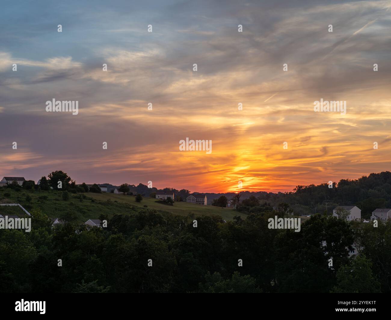 A vibrant sunset paints the sky above a suburban neighborhood, casting ...