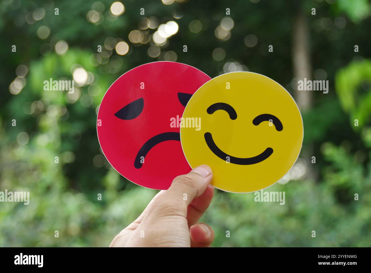 Hand holding a sad face card hiding behind a happy smiling face ...