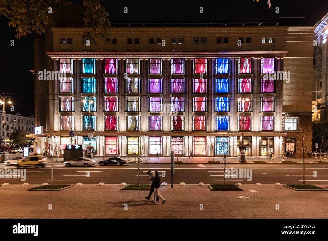 A building with colorful windows is lit up at night. A couple is ...