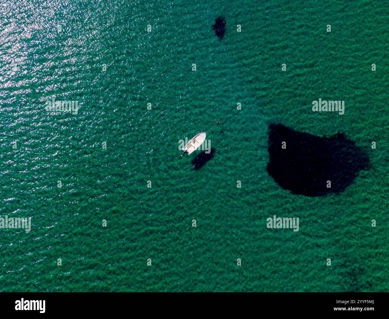 Aerial view of a small boat on a calm, teal sea. Dark underwater ...