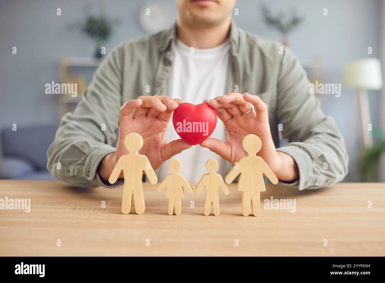 Man holding red heart above wooden family figures. Love, care ...