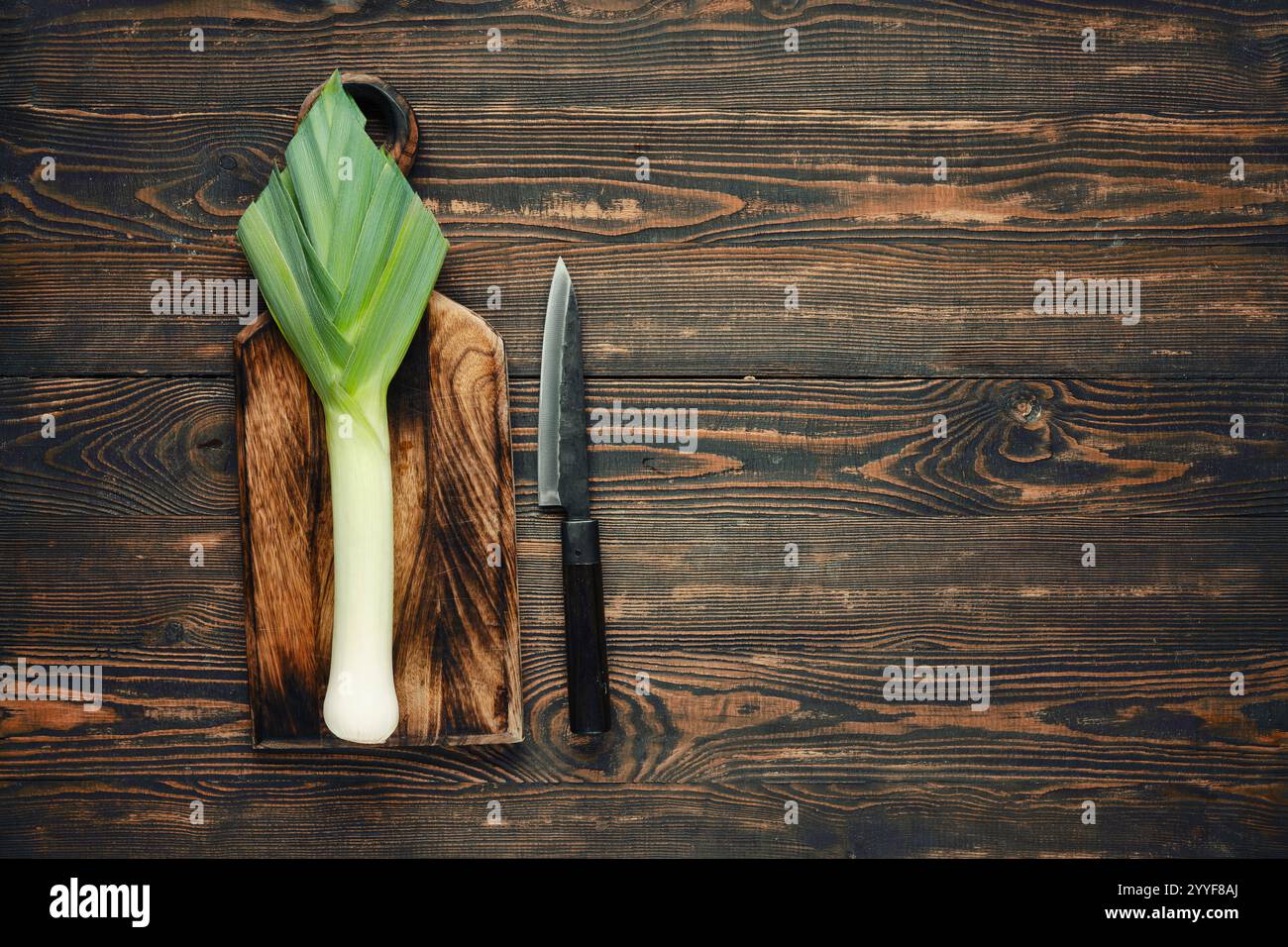 A fresh leek on a wooden chopping board beside a sharp knife, ready for ...
