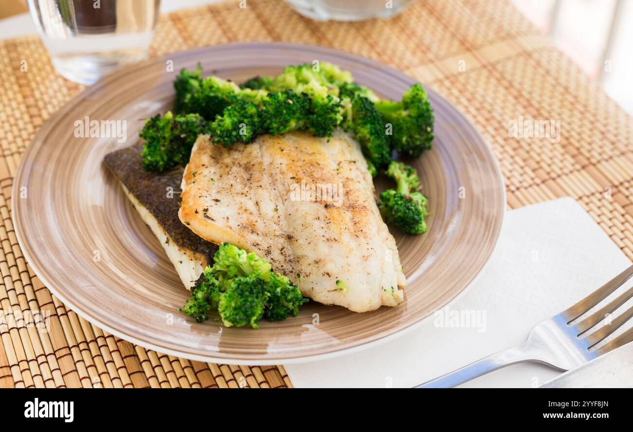Fried fillet of sea bass with garnish of broccoli on black warm stone ...
