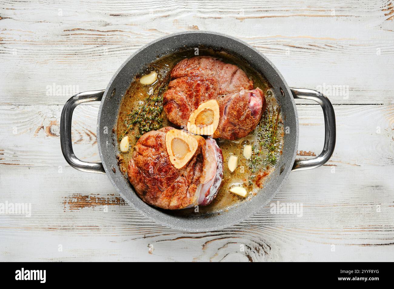 Two pieces of beef meat are being seared in a pan with garlic cloves ...