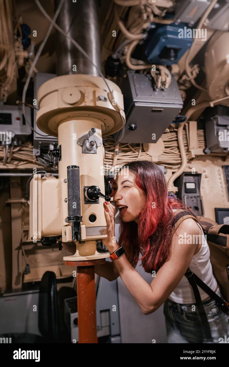 Young woman exploring submarine interior using periscope, experiencing ...