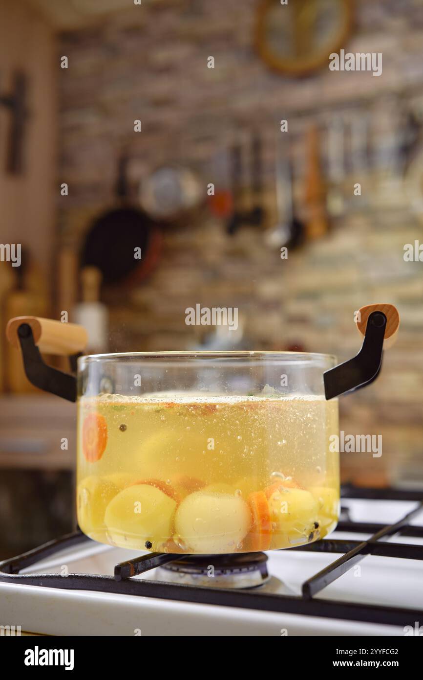 A clear pot filled with boiling water, potatoes, and carrots sits on a ...