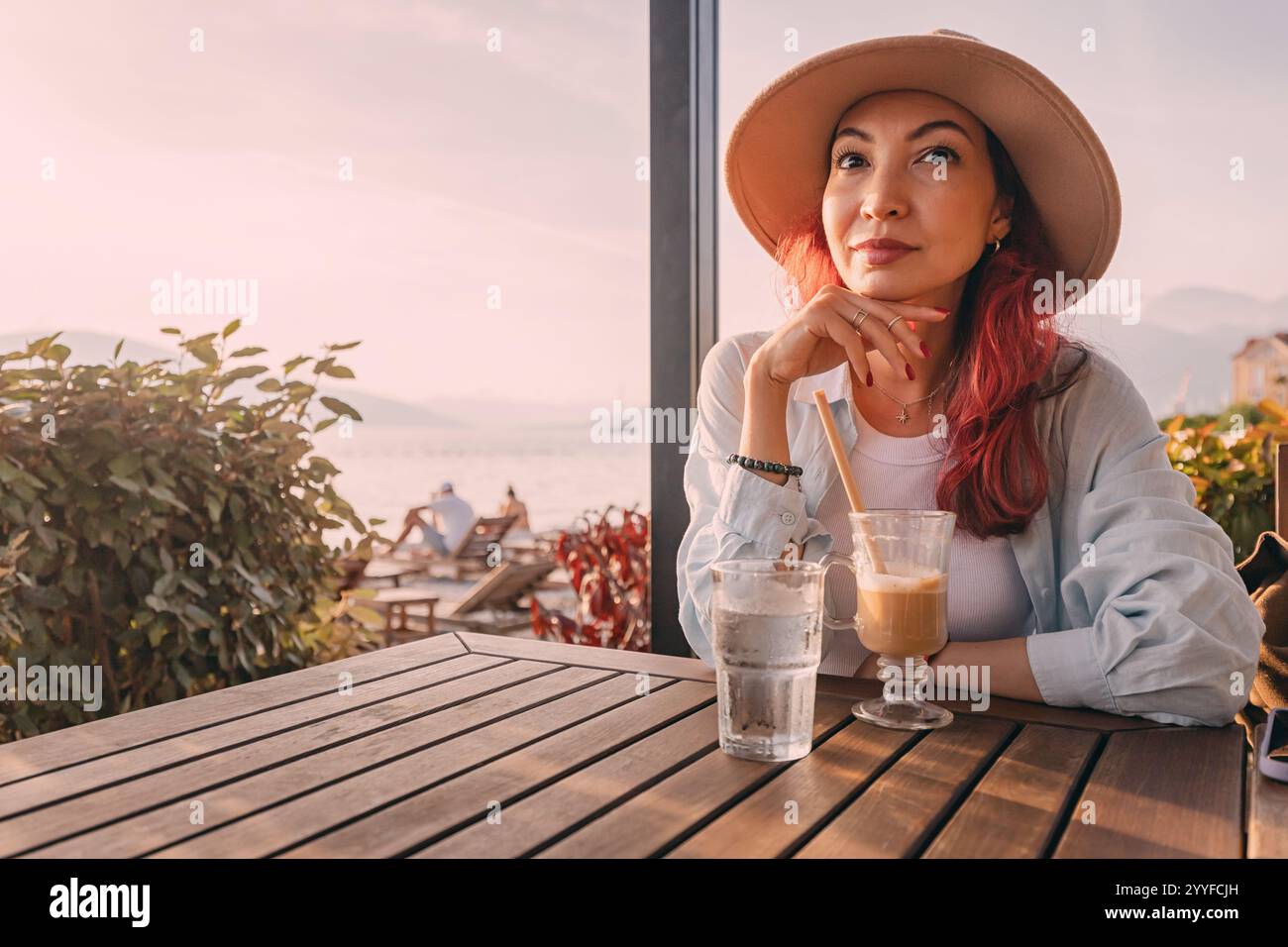 Stylish woman with hat enjoying a coffee break at a beach cafe during ...