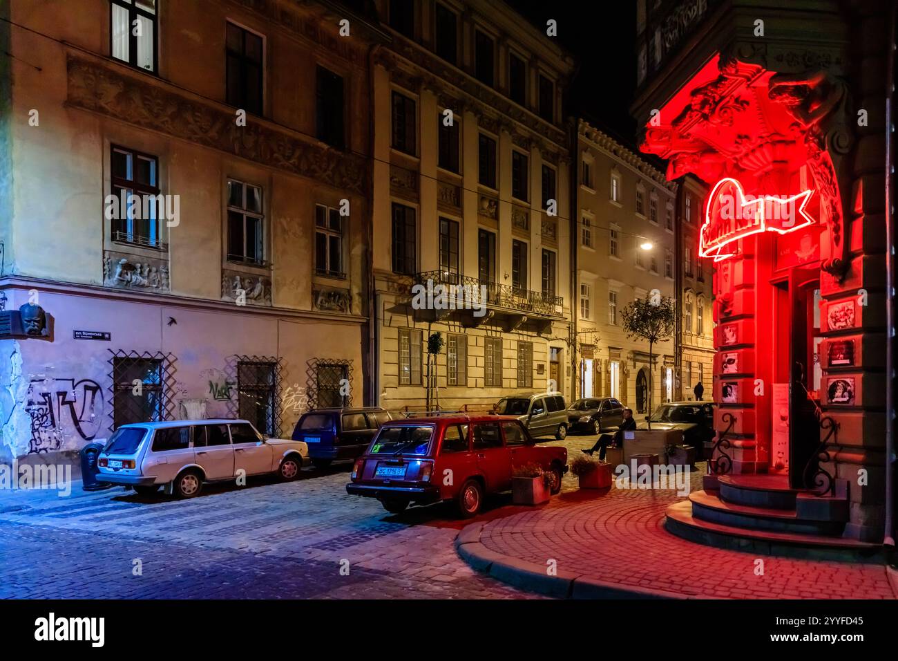A red neon sign is lit up on a dark street. The sign is on the side of ...