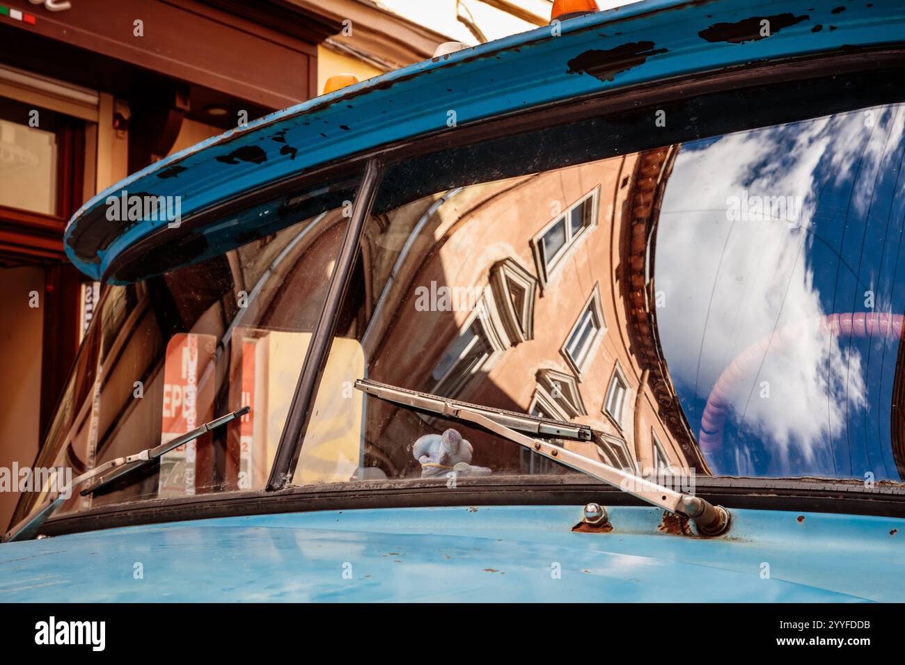 A blue car with a dirty windshield and a reflection of a building in ...