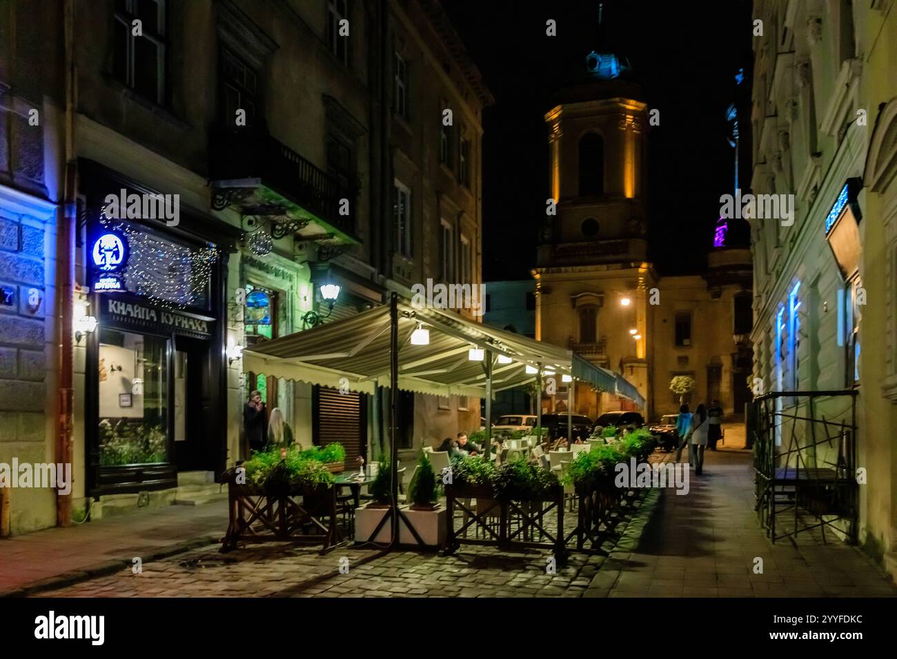 A city street at night with awnings over the tables and people sitting ...