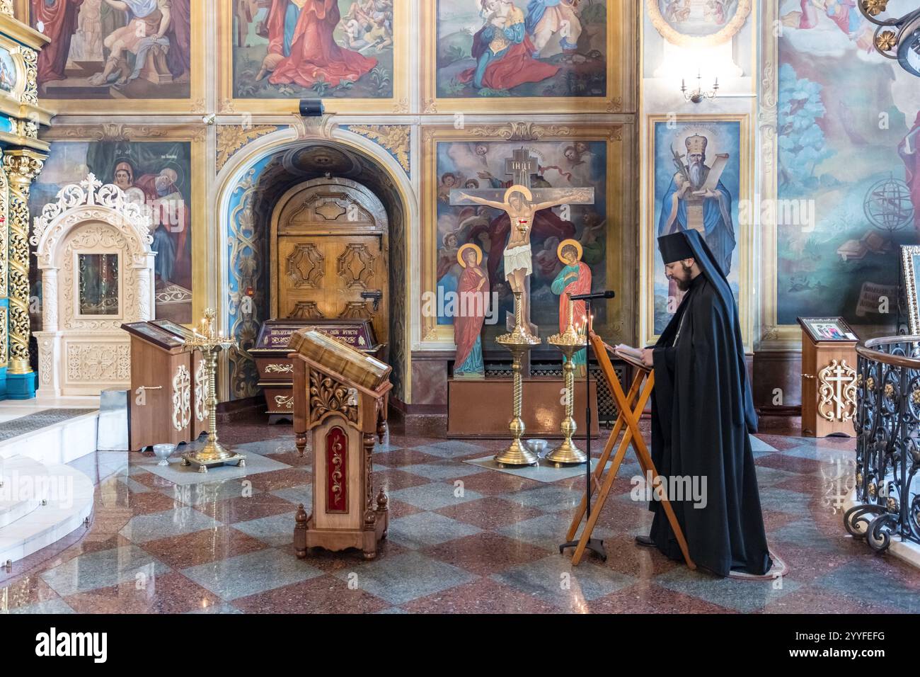 A man in a black robe stands in front of a large painting of Jesus ...