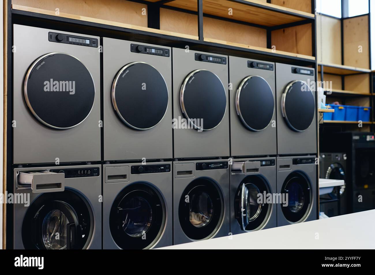 Double row of professional washing machines and coin operated clothes dryers at self service ...