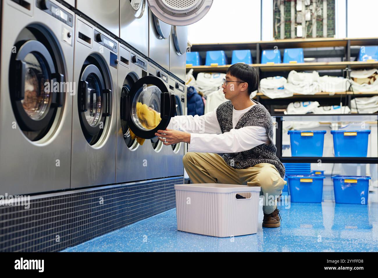 Side view of young Asian man loading clothes into washing machine from ...