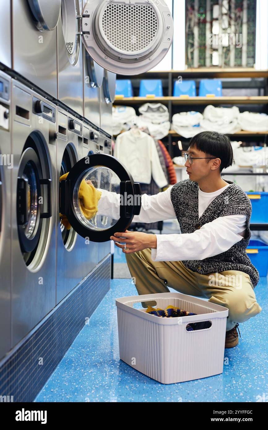 Vertical shot of male Asian customer unloading washing machine putting ...
