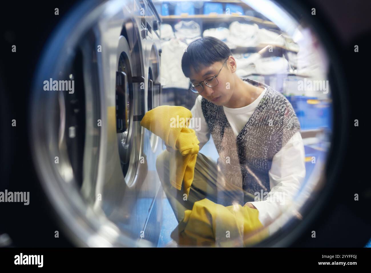 Shot through open washing machine of young Asian man unloading clean ...