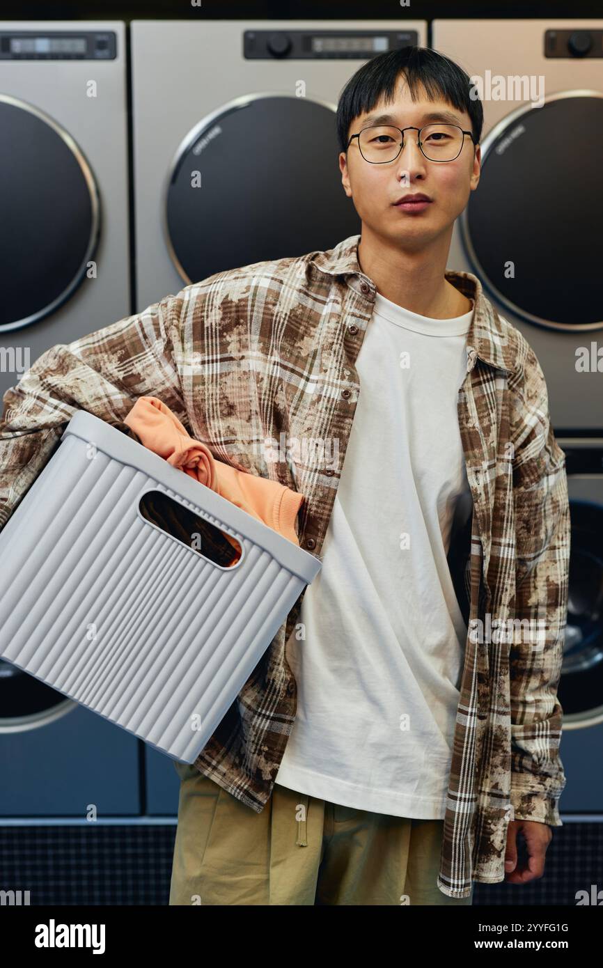 Vertical shot of young Asian man carrying basket with clothes preparing ...