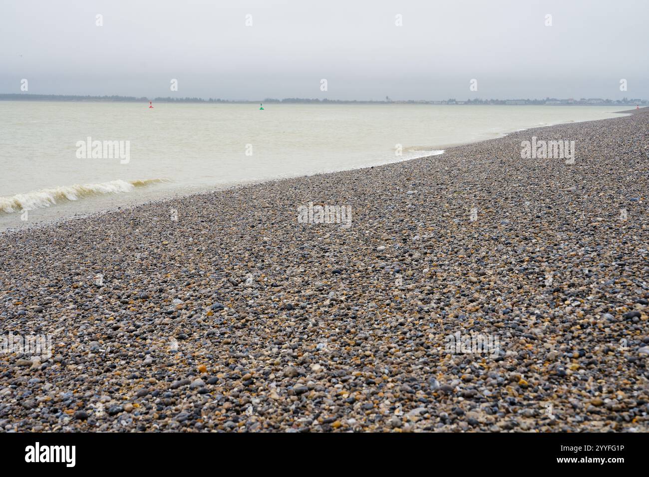 Coastal shoreline with pebbles and gentle waves under an overcast sky ...