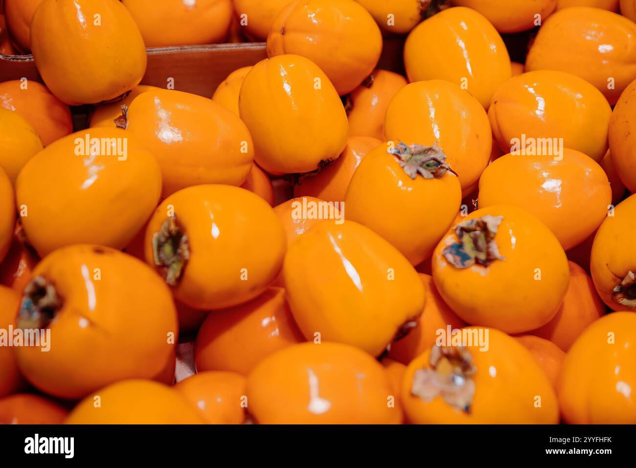 Pile of bright persimmons, a type of fruit, with some green leaves ...