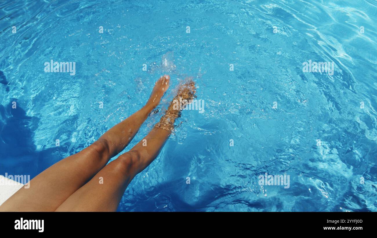 Woman is sitting at the edge of the pool with her legs dangling in the ...
