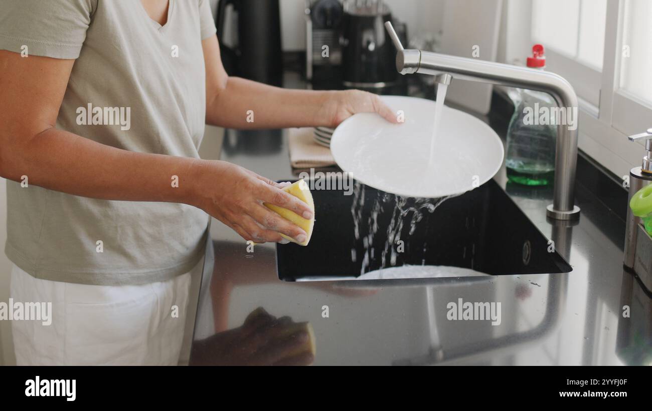 Woman washing and rinsing dishes by hand under a stream of water in the ...