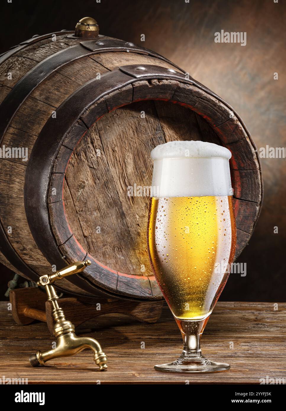 Glass goblet of chilled beer and wooden beer cask on the background ...